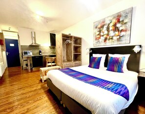 Quarto com cama grande, piso de madeira, cozinha compacta e closet espaçoso.