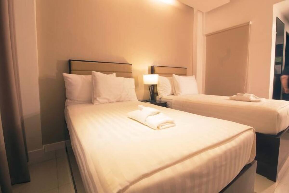 Quarto de hotel com duas camas, uma mesa de cabeceira, um abajur e uma porta.