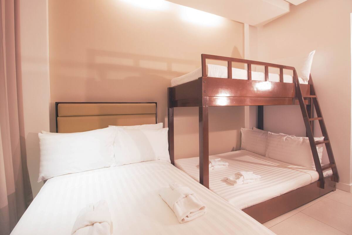 Quarto de hotel com duas beliches, uma cabeceira de madeira e uma escada.