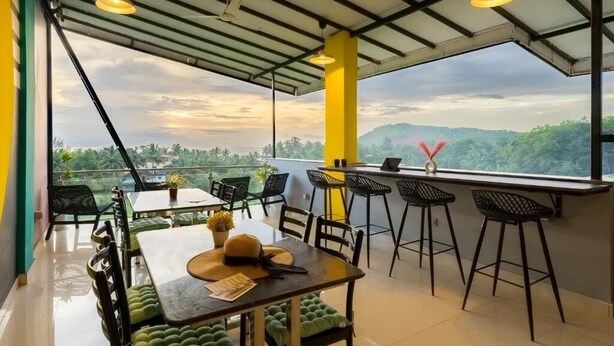 Uma área de refeições com mesa e cadeiras, um espaço bar com banquetas e vista para a paisagem.