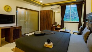 Quarto de hotel com uma cama, televisão, guitarra, relógio e janela com vista para o verde.