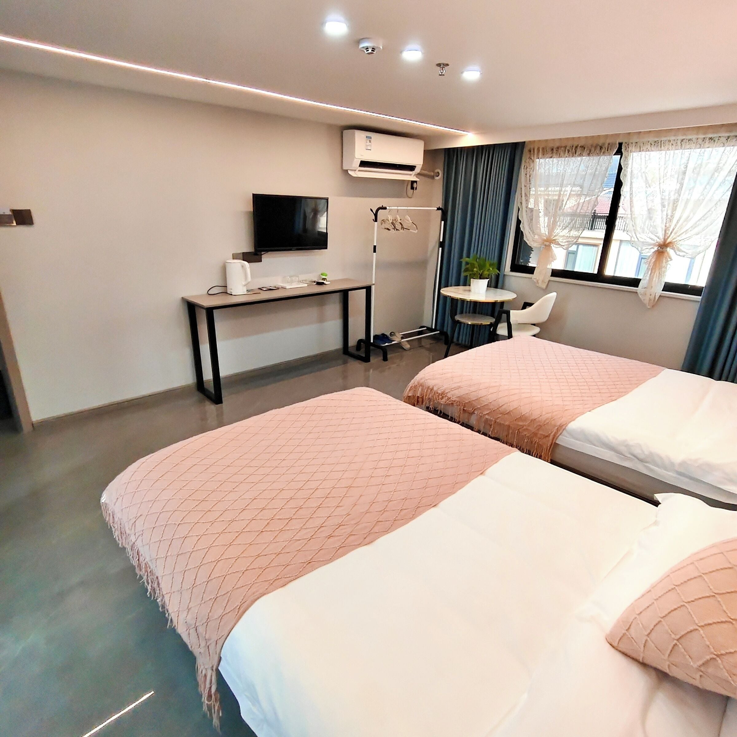 Quarto de hotel com duas camas, uma escrivaninha, televisão e janela com cortinas.
