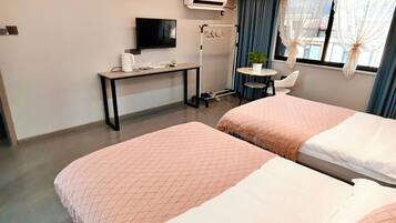 Quarto de hotel com duas camas, uma escrivaninha, televisão e janela com cortinas.