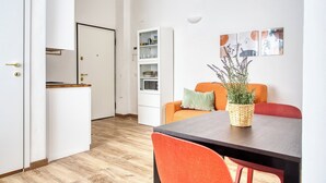 Uma sala de estar moderna com uma mesa de jantar, cadeiras laranja, um armário branco e uma planta em vaso.