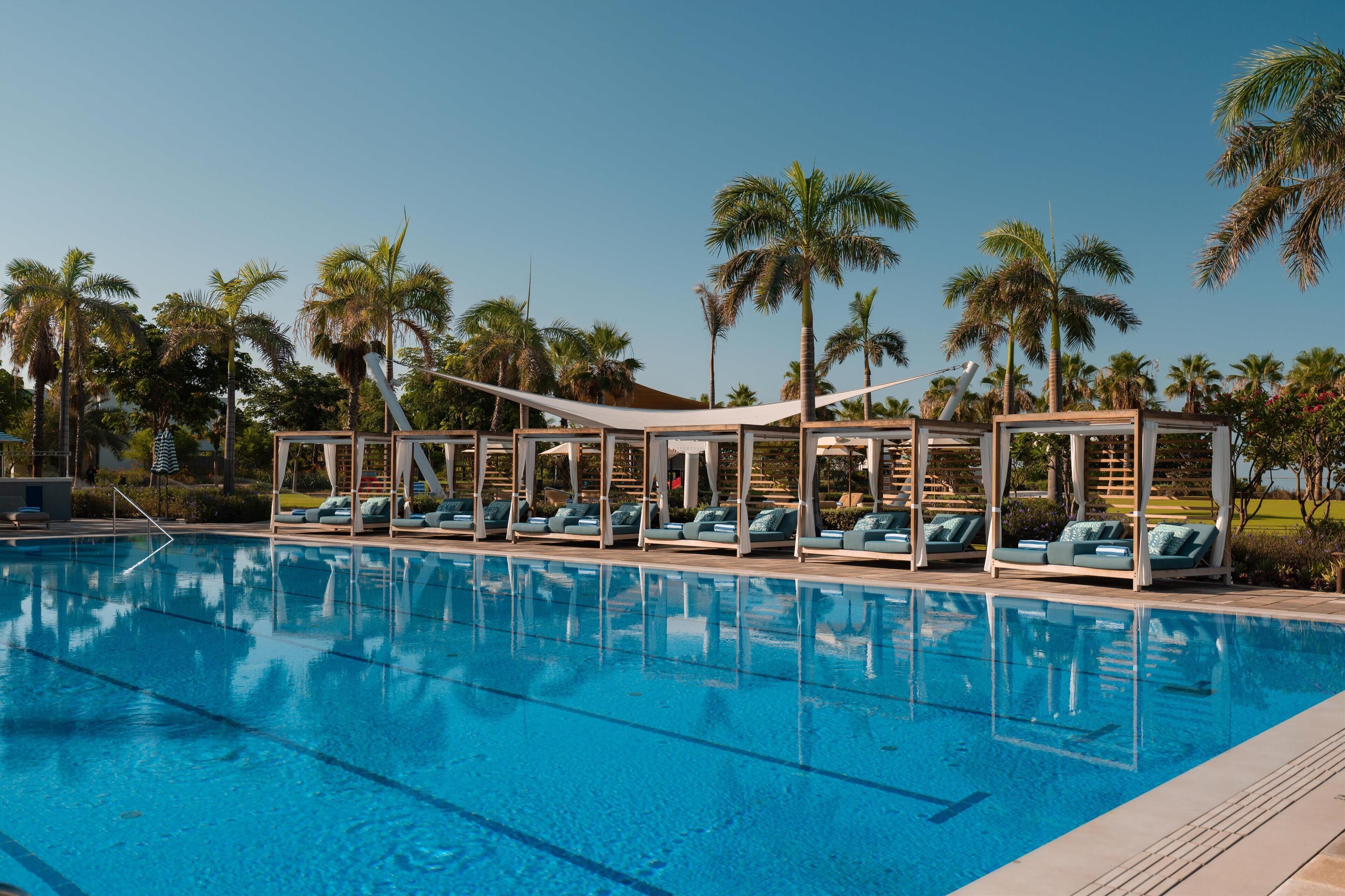 Piscina com espreguiçadeiras e palmeiras ao fundo.