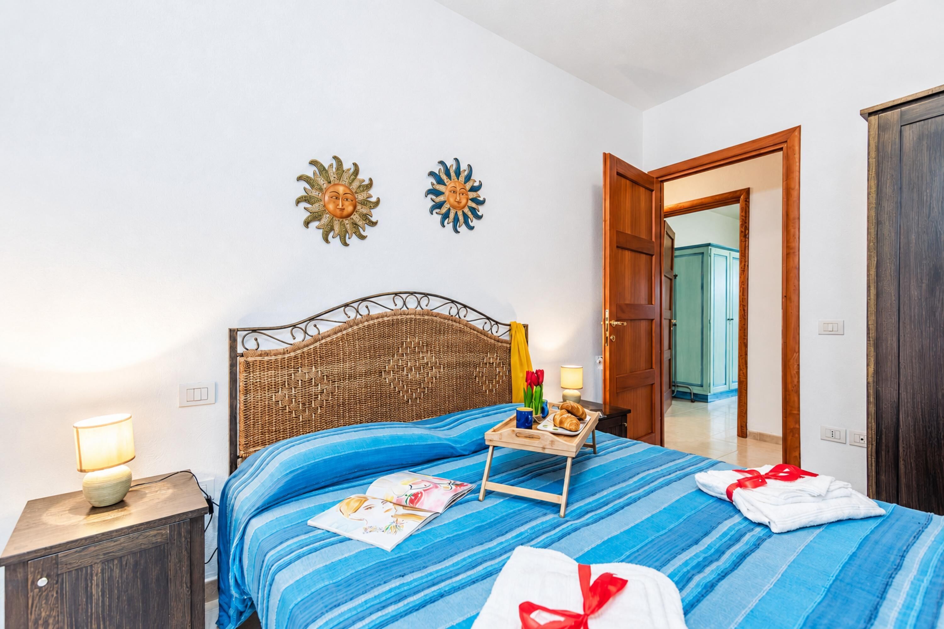 Quarto de hotel com cama, mesa de cabeceira e porta que dá para outro espaço.