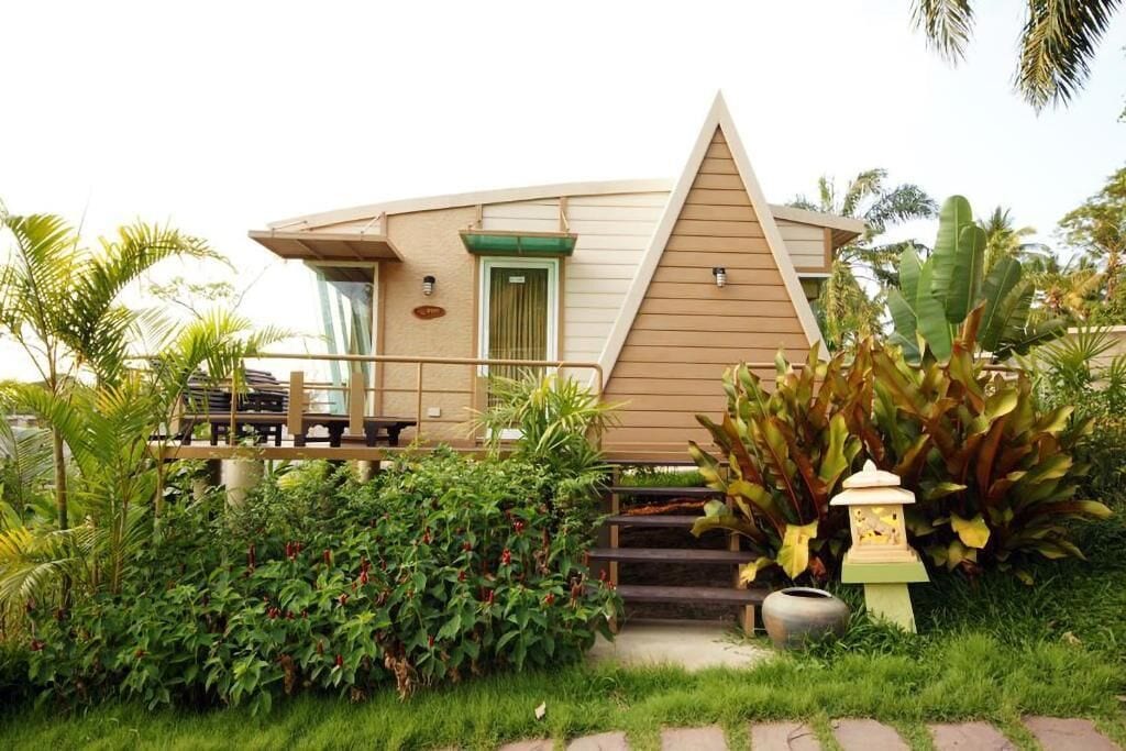 Um edifício térreo com telhado triangular, porta verde e uma pequena varanda com um banco.