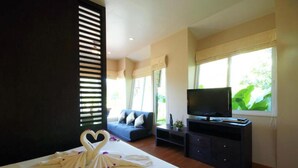 Quarto de hotel com cama, televisão, sofá e janela com vista para o verde.