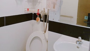 Casa de banho com sanita, lavatório e chuveiro. Produtos de higiene pessoal numa prateleira e um espelho na parede.