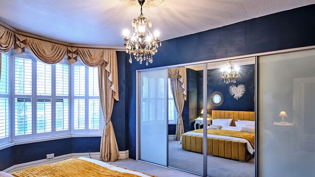 Quarto com uma cama grande, um candelabro e uma porta de vidro deslizante que dá para um banheiro.