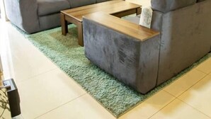 Uma sala de estar com sofá modular cinza, mesa de centro de madeira e tapete verde.