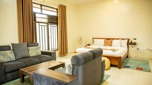 Quarto de hotel com cama, sofá, mesa de centro e janela com cortinas.