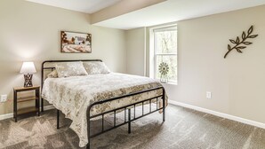 Um quarto com cama, mesa de cabeceira, luminária, janela e um ornamento na parede.