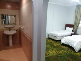 Quarto de hotel com banheiro, incluindo pia e espelho, duas camas com roupa de cama branca e um tapete verde estampado.