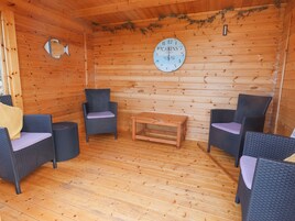 Interior de uma cabana de madeira com cadeiras de vime, uma mesa de madeira e uma decoração de peixe na parede.