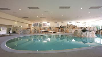 Piscina interna com paisagem rochosa ao fundo, parede de vidro e escadaria para um andar superior.