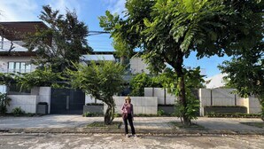 Uma pessoa em um espaço pavimentado, com árvores e edifícios ao fundo.