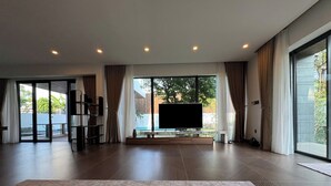 Uma sala de estar ampla com uma grande TV de tela plana, uma estante embutida e uma porta de vidro que se abre para uma área externa.