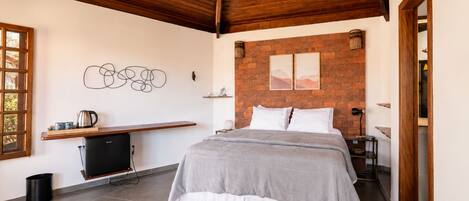 Quarto com cama, escrivaninha, parede de tijolos e janela.