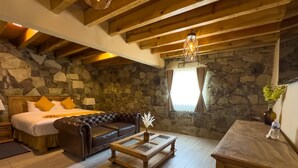 Um quarto acolhedor com parede de pedra, teto de madeira, cama com almofadas amarelas, sofá de couro e mesa de centro de madeira.
