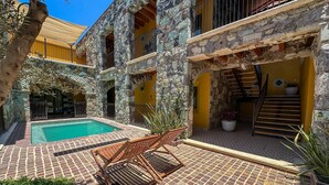 Pátio com piscina, paredes de pedra e escadaria de madeira.