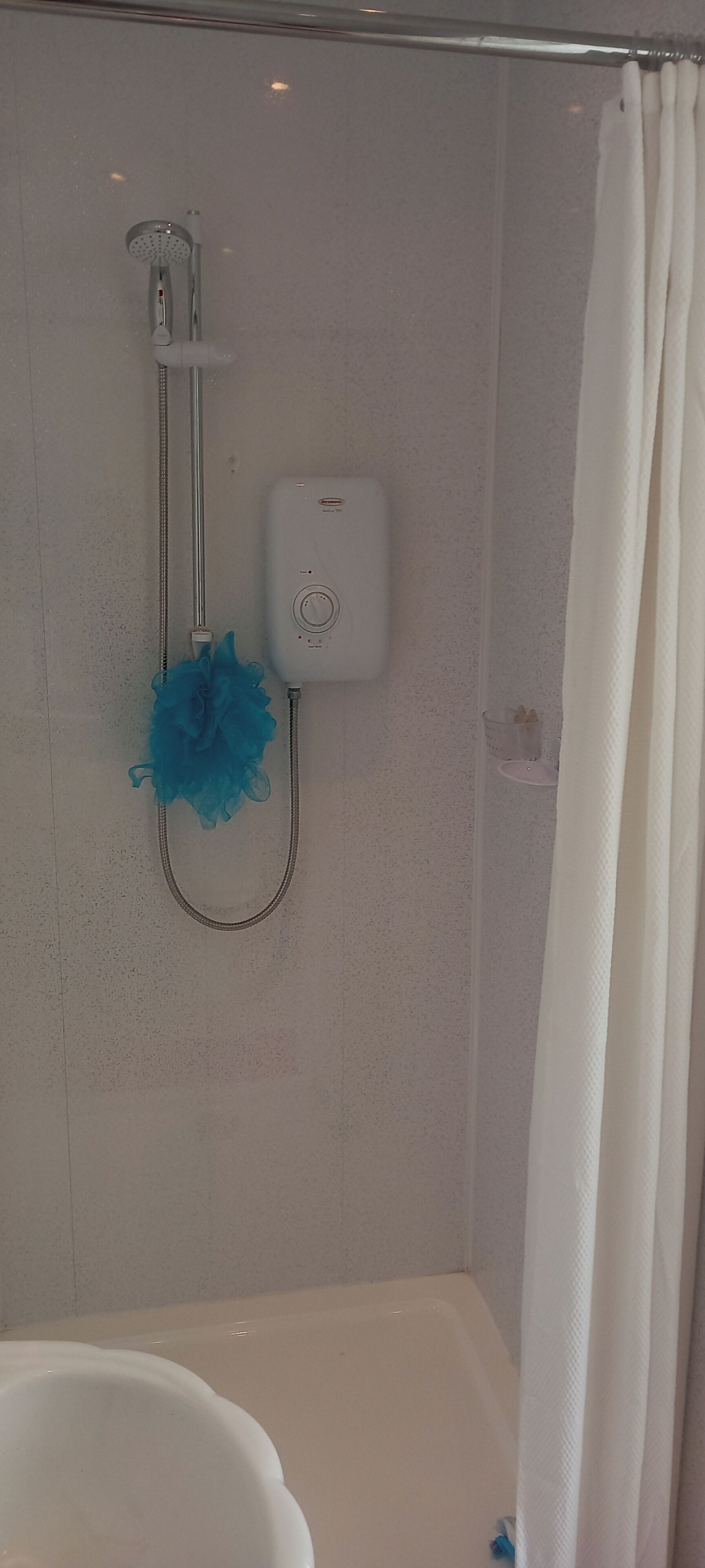 Chuveiro com chuveiro manual, painel de controle fixado na parede e capa azul para o chuveiro.