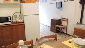 Cozinha compacta com micro-ondas, geladeira e armários de madeira. Uma mesa de jantar com cadeiras e uma tigela de vidro estão visíveis.