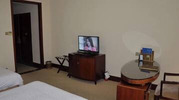 Quarto de hotel com televisão sobre um armário de madeira, uma mesa redonda e duas camas.
