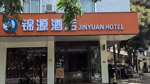Exterior do Hotel Jinyuan, com uma placa chamativa, portas de entrada e uma pequena área de estar ao ar livre visível através das portas de vidro.