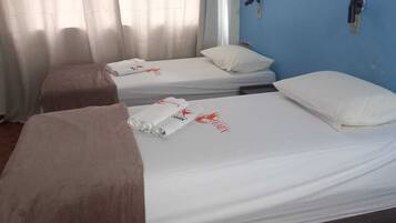 Quarto de hotel com duas camas de solteiro, cada uma com colcha branca e toalha enrolada.