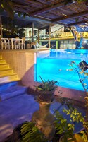 Uma área de piscina com teto de bambu, assentos externos e uma escadaria que leva a um andar superior.