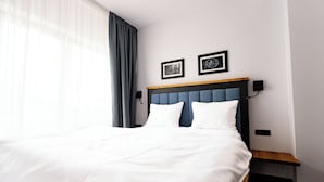 Cama bem arrumada com lençóis brancos, cabeceira estofada em azul e duas molduras com quadros na parede.