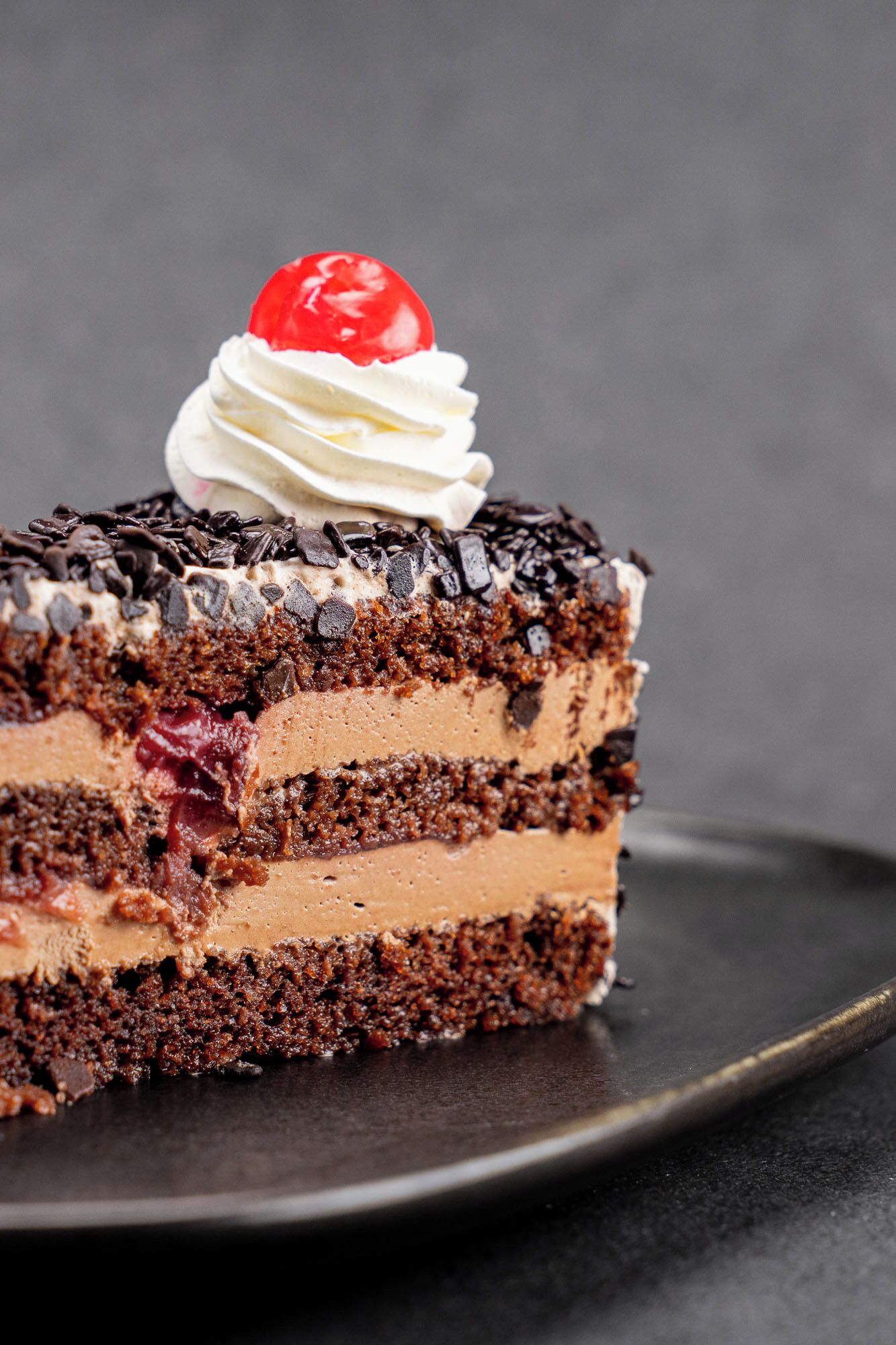 Uma fatia de bolo de chocolate com camadas, chantilly e uma cereja por cima.
