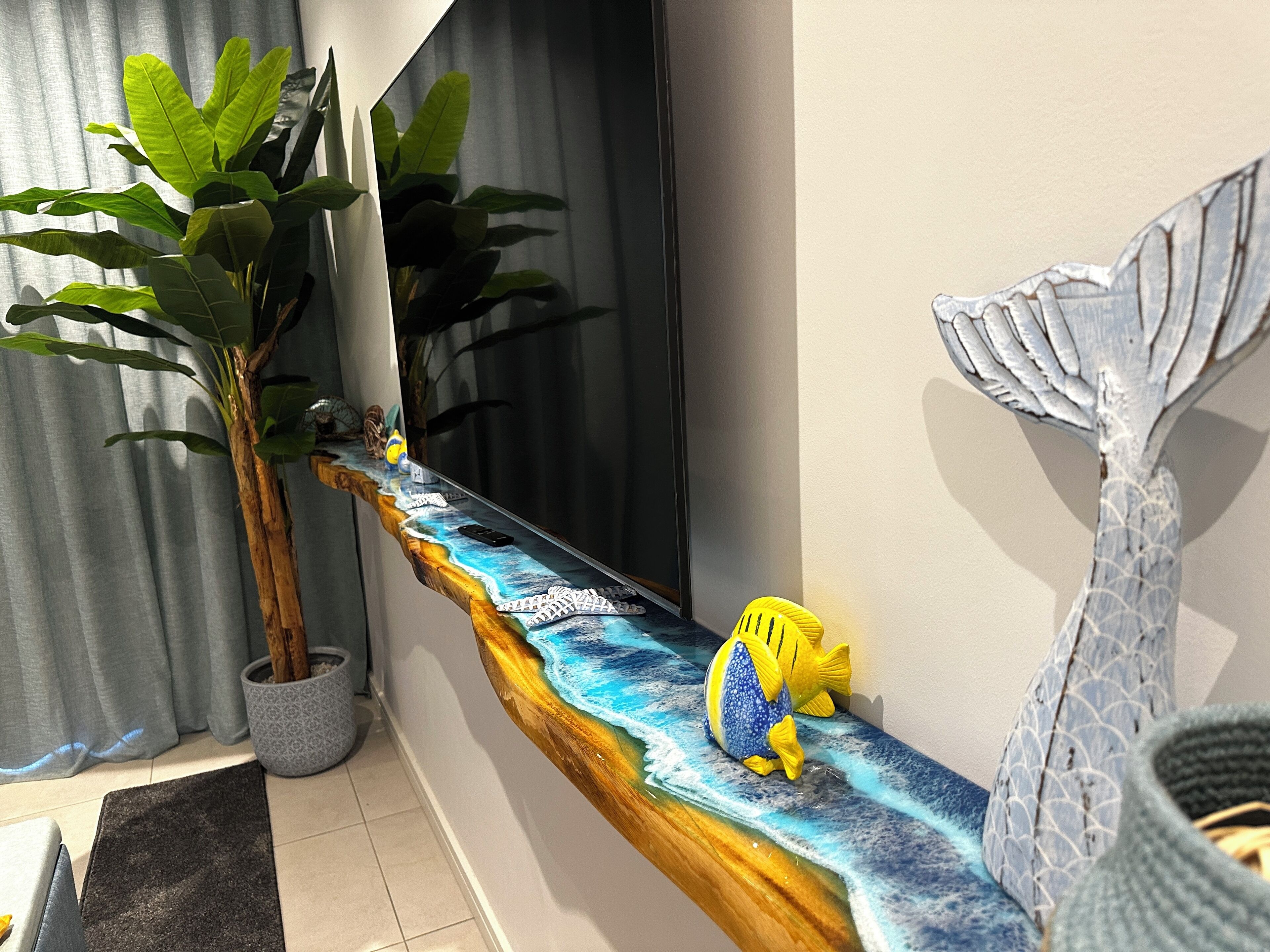 Estante de madeira com um desenho azul e branco, um vaso com planta e uma estatueta de peixe amarelo.