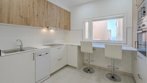 Uma cozinha moderna com armários brancos, lava-louças embutida, janela com vista e dois bancos altos.