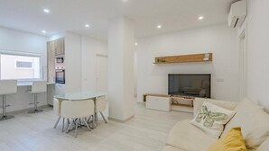 Um apartamento moderno com área de jantar, cozinha compacta, sala de estar e TV.