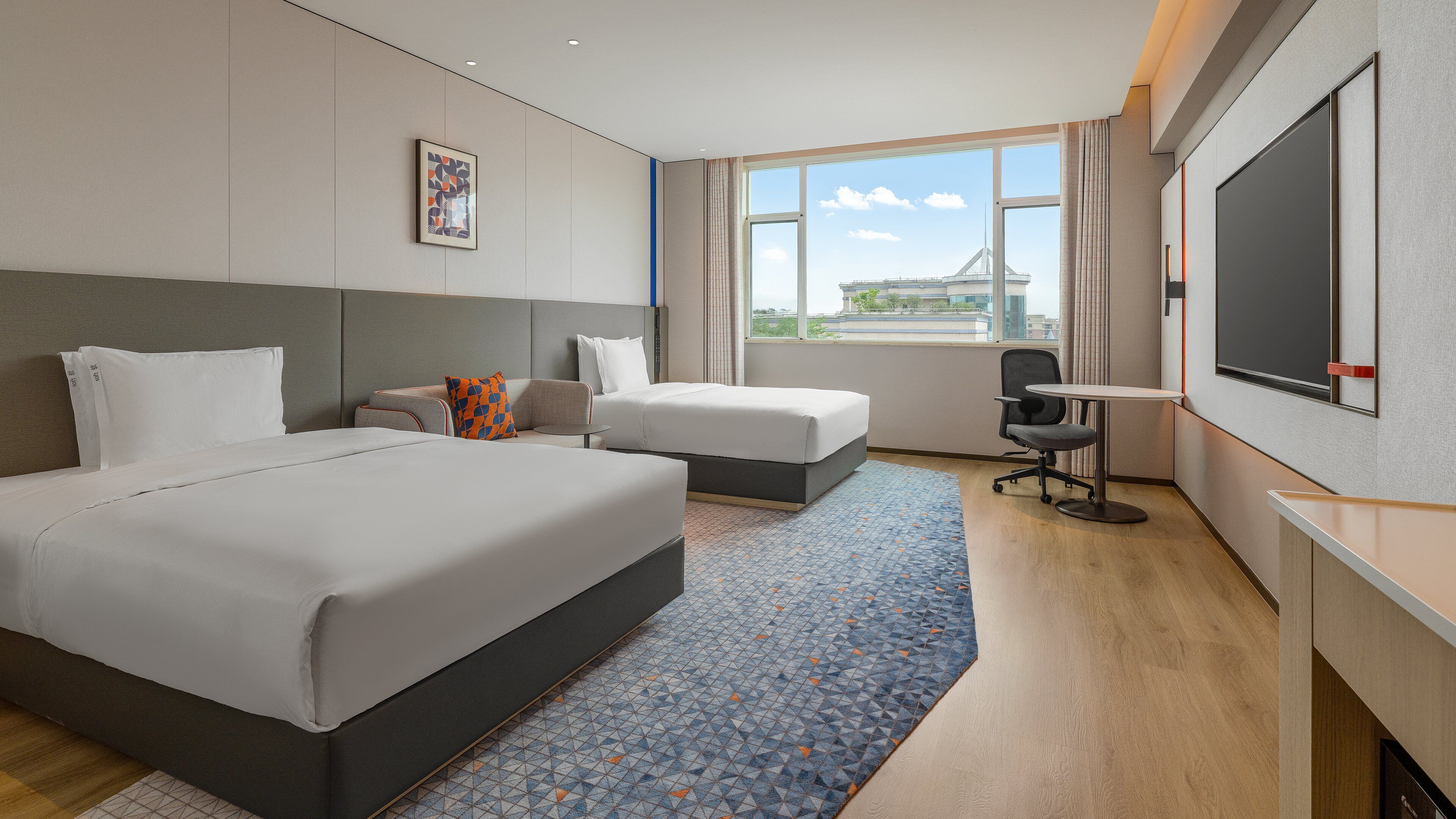 Quarto de hotel com uma cama grande, uma cama menor, uma escrivaninha e uma televisão.