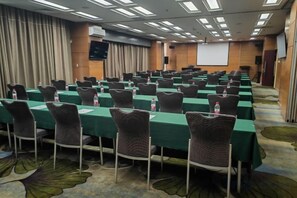 Sala de conferências com várias mesas e cadeiras, uma tela de projetor e piso coberto por carpete.