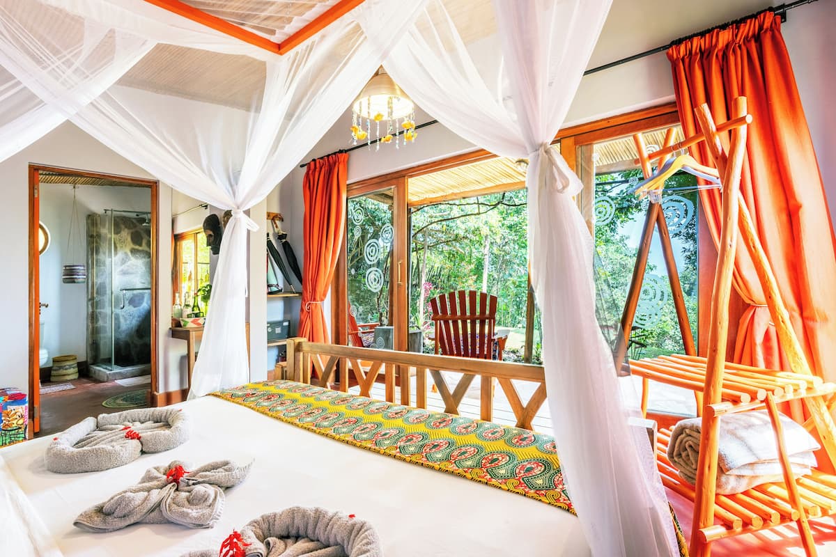Quarto com cama, cadeira de balanço de madeira, cadeira suspensa e vista para o exterior.