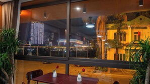 Restaurante com grandes janelas que oferecem vista para a cidade à noite.