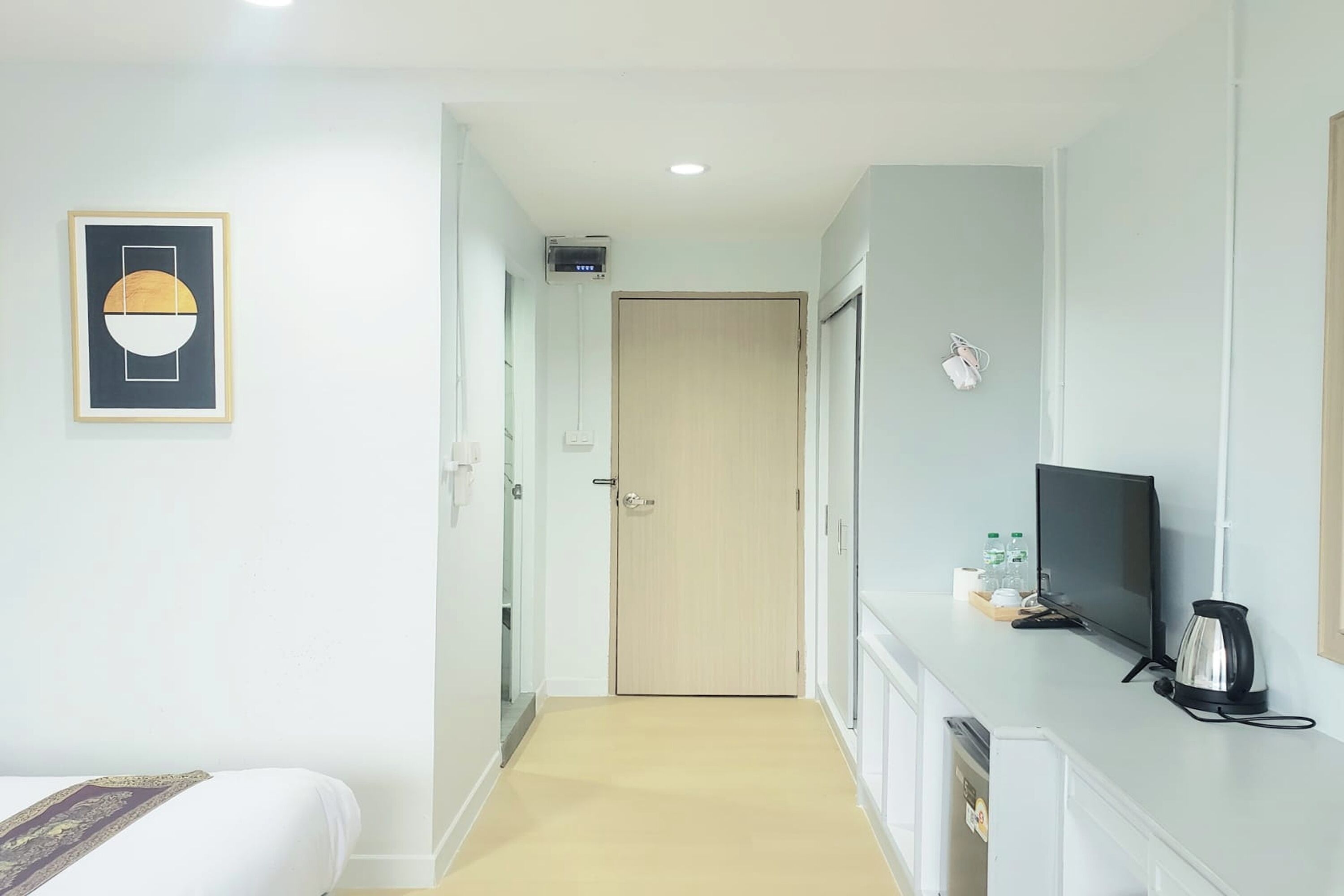 Quarto de hotel com cama, televisão, cafeteira e porta que dá para outro cômodo.