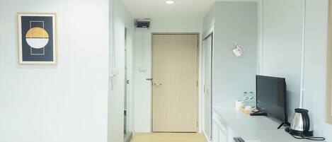 Quarto de hotel com cama, televisão, cafeteira e porta que dá para outro cômodo.