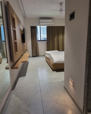 Quarto de hotel com cama, televisão na parede, janela com cortinas e aparelho de ar condicionado.