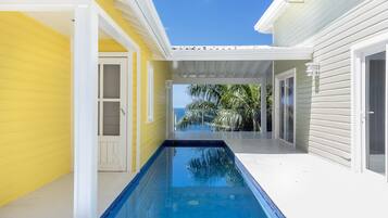 Uma área de piscina moderna com vista desobstruída do oceano, rodeada por edifícios amarelos e brancos.