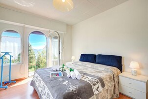 Quarto com cama, mesa de cabeceira, luminária, janela com vista e porta-toalhas.