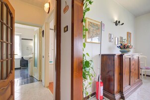 Um corredor com porta de madeira, uma planta, um armário e uma cadeira.