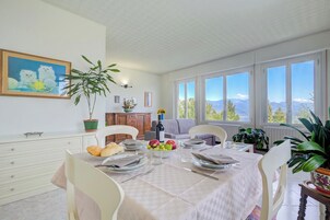 Uma sala de jantar com mesa posta para quatro pessoas, um quadro na parede e vista para as montanhas por grandes janelas.