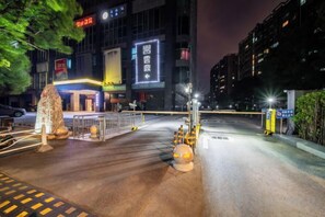 Cena urbana noturna com um edifício, letreiros iluminados e entrada protegida por grades.