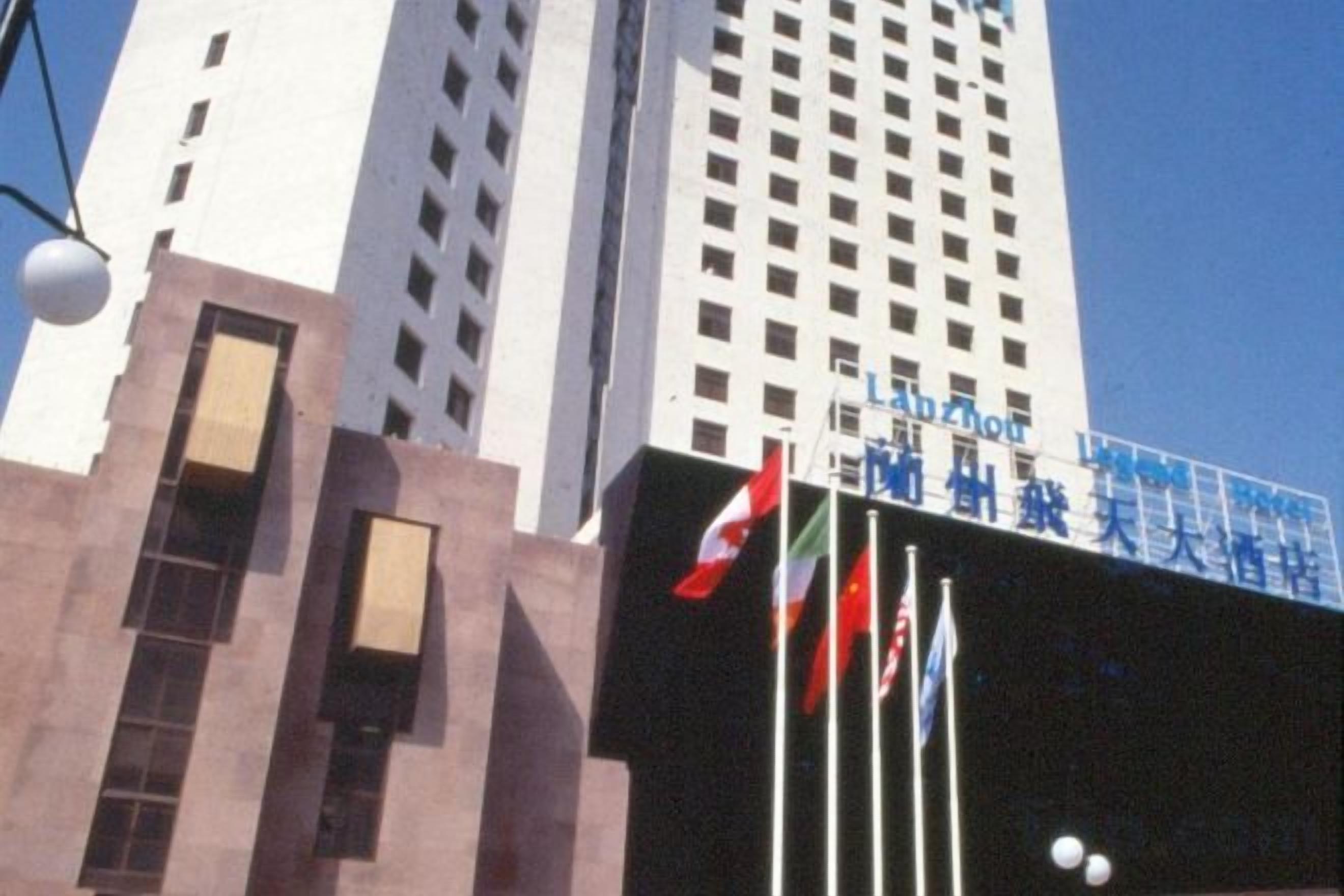 Um edifício alto com várias bandeiras, incluindo a bandeira dos Emirados Árabes Unidos, e uma placa com caracteres chineses.