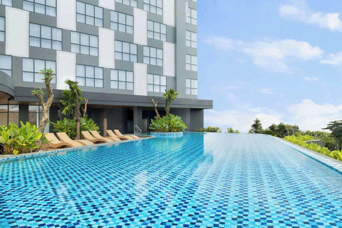 Um hotel moderno com piscina, espreguiçadeiras e palmeiras.